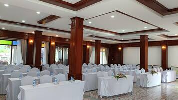 Sala de conferência com várias mesas, cadeiras brancas e garrafas de água.