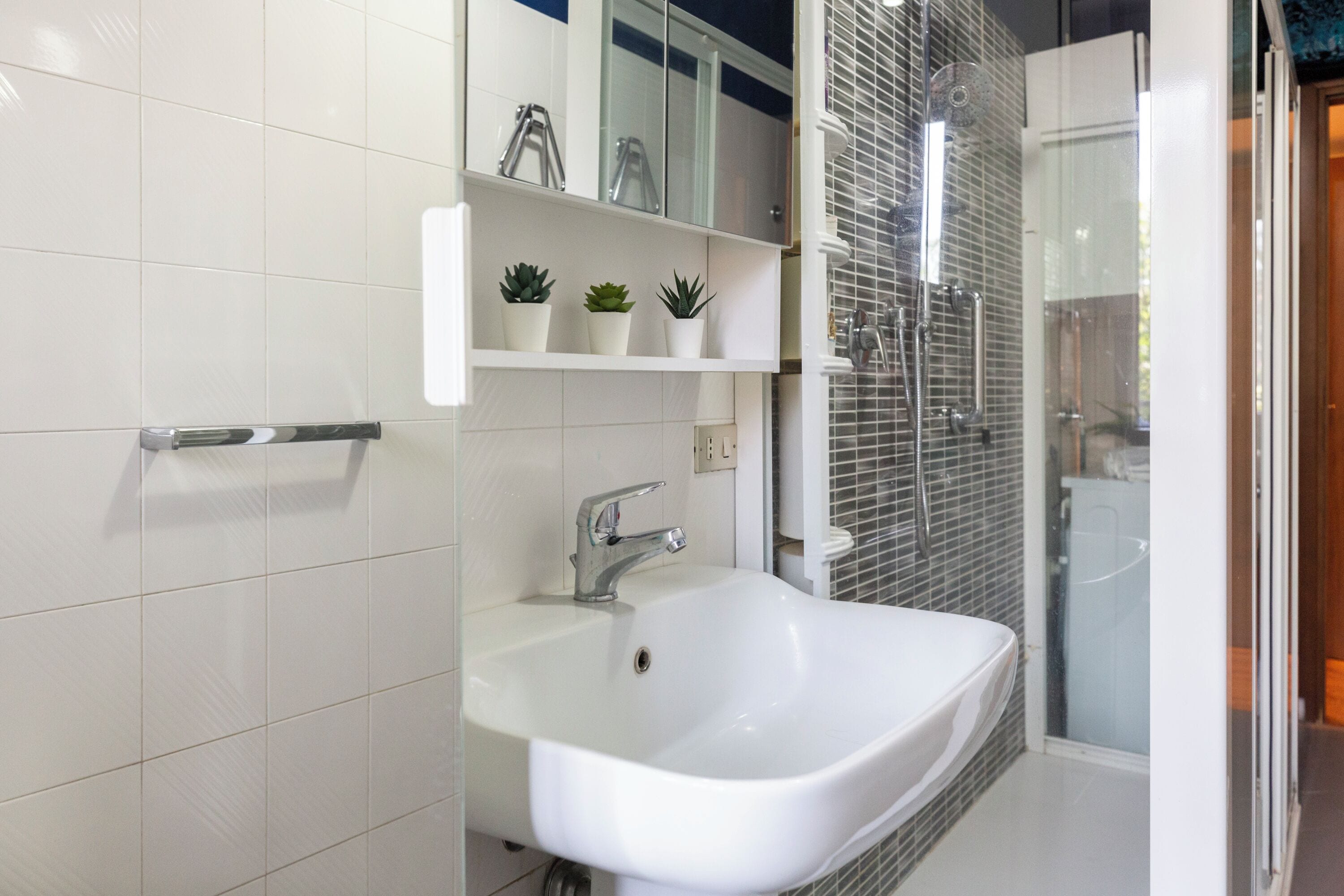 Uma casa de banho moderna com uma pia branca, um espelho e zona de duche.