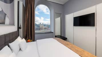 Quarto de hotel moderno com uma cama grande, televisão, guarda-roupa e janela com vista para a cidade.