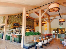 Um restaurante com vigas de madeira altas, luminárias pendentes e um bar com prateleiras cheias de garrafas.