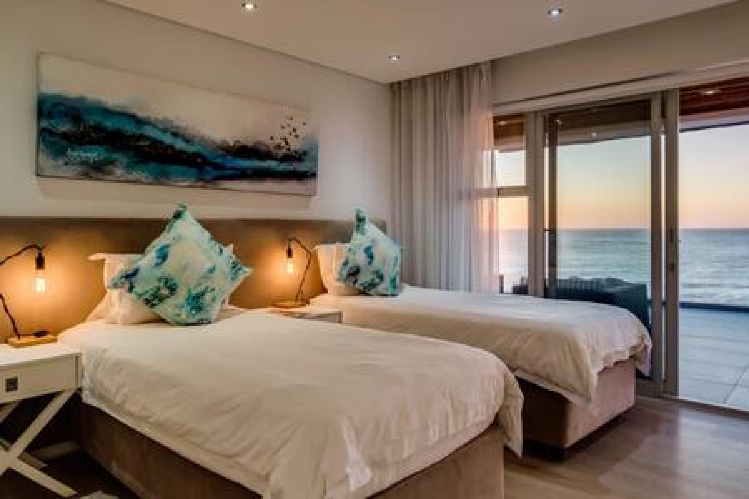 Quarto de hotel moderno com duas camas, uma janela ampla com vista para o mar e um quadro na parede.