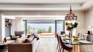 Uma sala de estar moderna com sofá, mesa de jantar e cadeiras, uma janela grande com vista para o verde, e uma luminária pendente.
