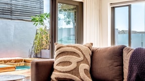 Uma sala de estar moderna com um sofá, uma almofada decorativa, um vaso e vista para o exterior através de grandes janelas.