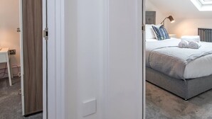 Quarto com claraboia, cama com almofadas, mesa de cabeceira e abajur.