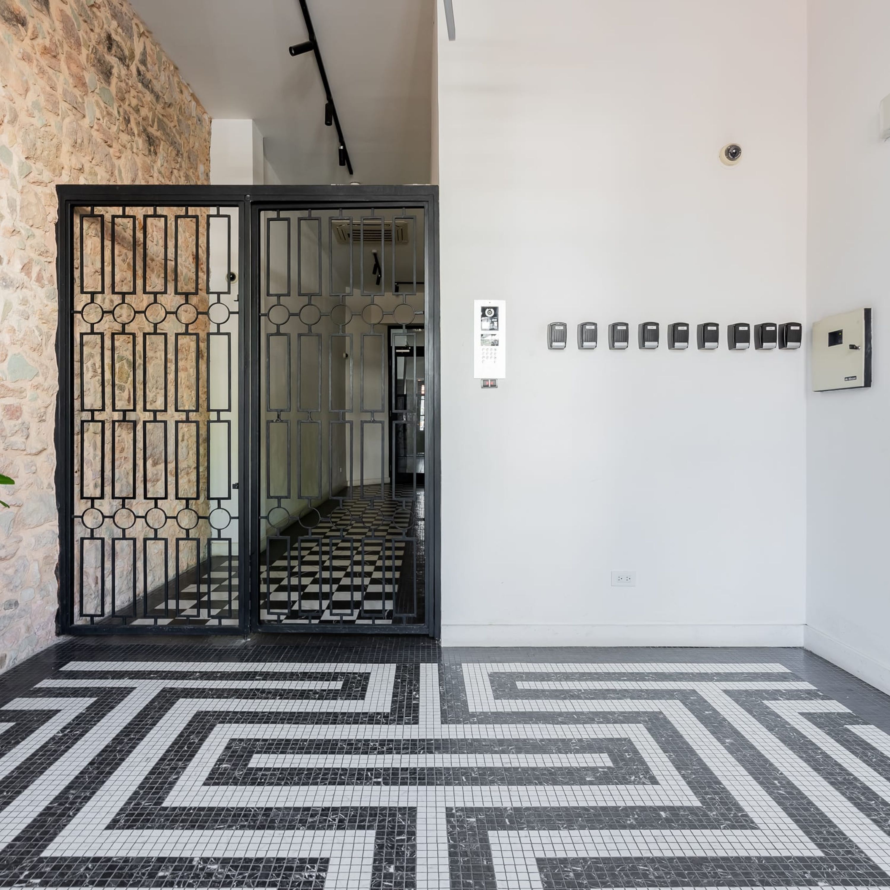 Um corredor com piso de padrão geométrico, parede de pedra e porta com grade de metal.