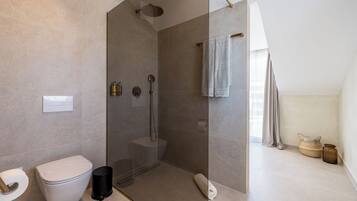 Uma casa de banho moderna com chuveiro separado por vidro, sanita e lavatório.
