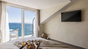 Quarto com uma cama grande, televisão na parede e varanda com vista para o mar.
