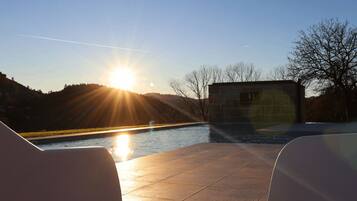 Área da piscina com um edifício de pedra com a inscrição 'Casa d'Heritage' e vista para o pôr do sol sobre a água.