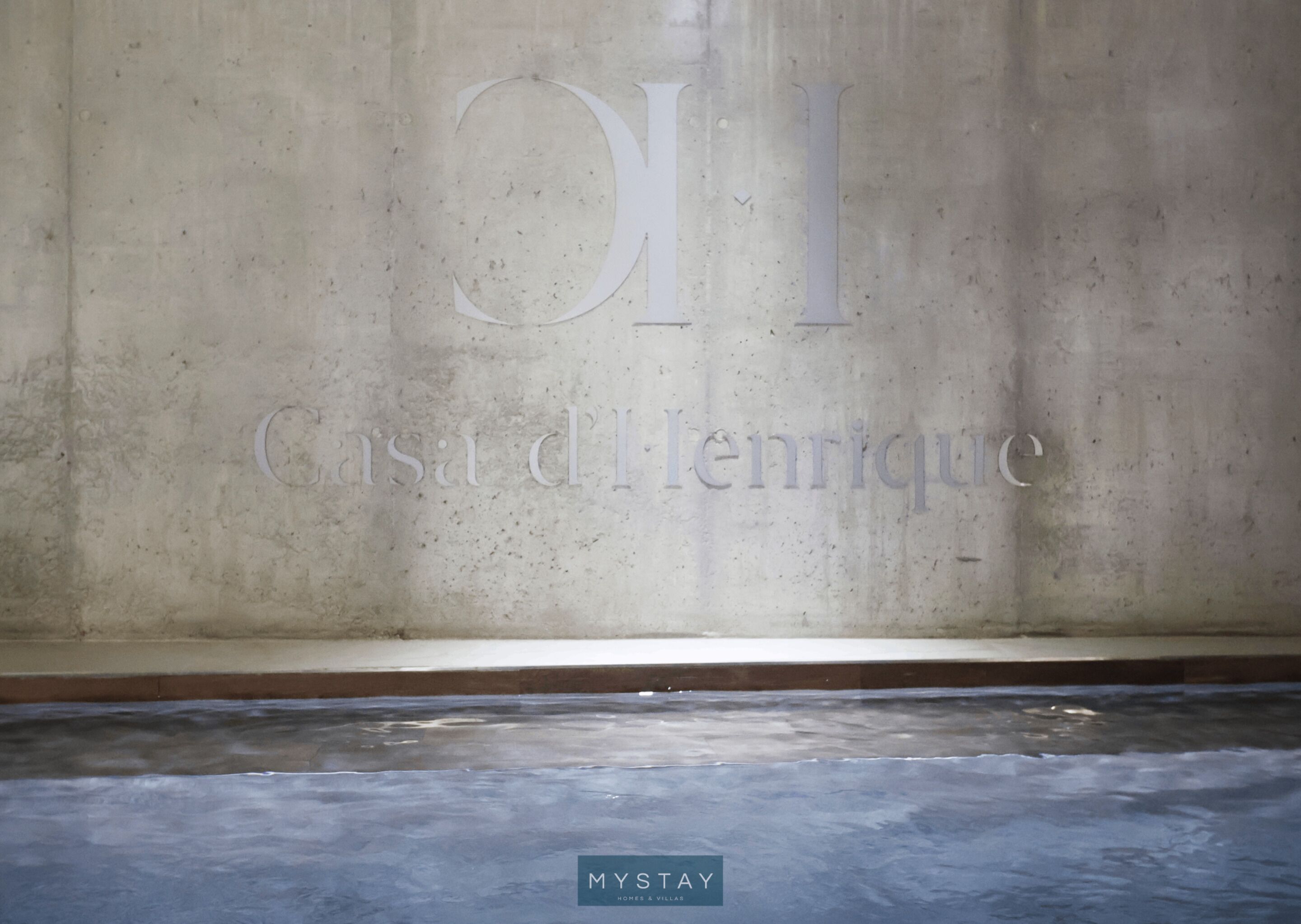 Parede de concreto com o texto "Casa d'lenrique" e "MYSTAY HOMES & VILLAS" visível.