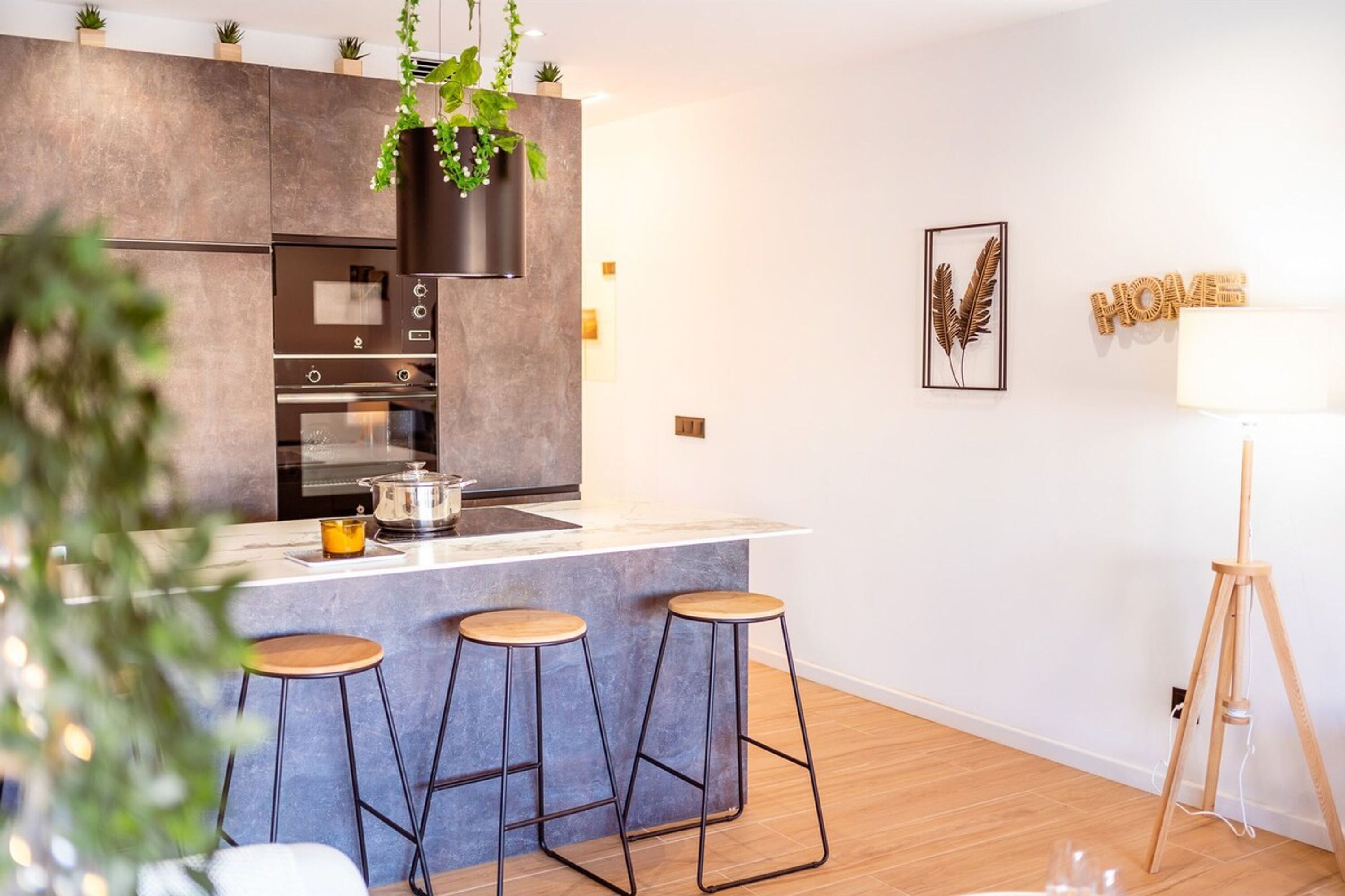 Uma cozinha moderna com uma ilha central, banquetas de bar e uma planta pendurada.