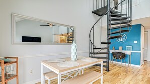 Cozinha moderna com uma mesa de madeira, banco e um espelho grande. Uma escada em caracol é visível ao fundo.
