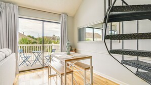 Quarto moderno com mesa de jantar de madeira, sofá e varanda com vista para casas.