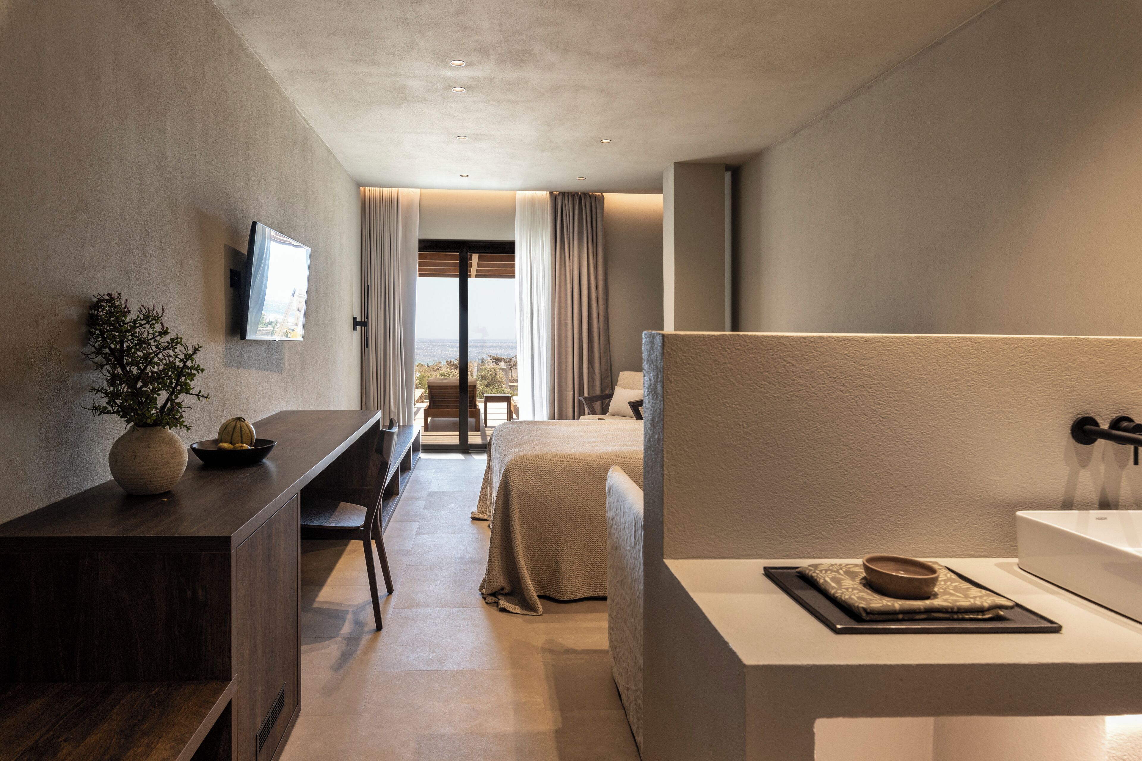 Quarto de hotel moderno com cama, escrivaninha, televisão e vista da cidade.