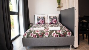 Quarto moderno com cama, roupa de cama floral, mesa de cabeceira e vista pela janela.