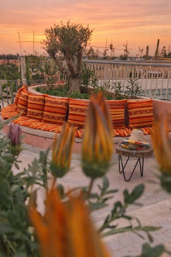 Vista do pôr do sol com um sofá curvo e uma mesa pequena em um jardim.