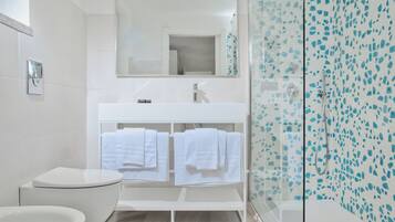 Casa de banho moderna com lavatório branco, sanita e cabine de duche com mosaicos.
