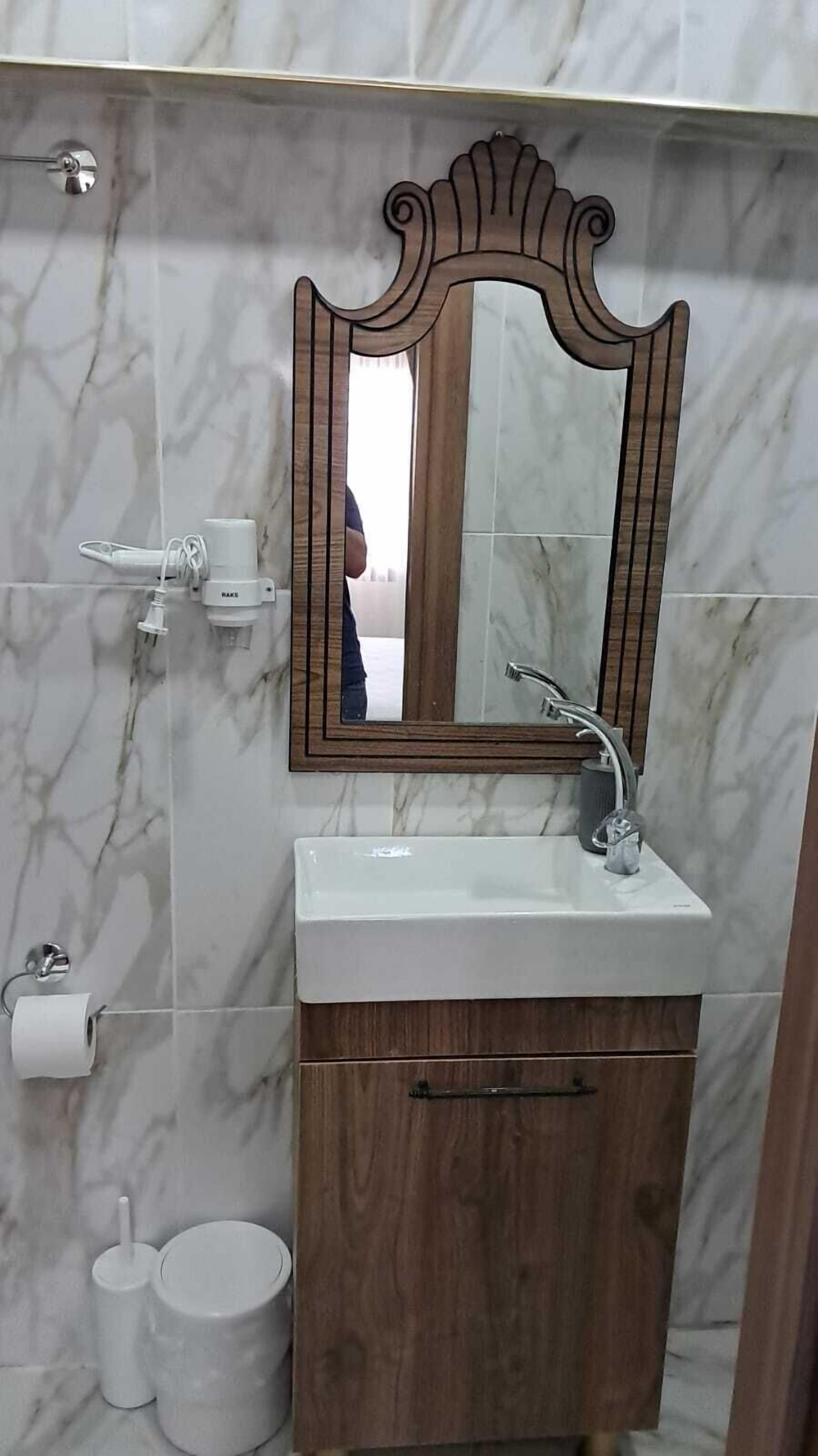 Casa de banho com parede em azulejo de mármore, toucador de madeira com lavatório, espelho e porta-papel higiénico.