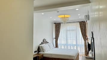 Quarto com uma cama grande, piso de madeira, um candelabro e uma janela com cortinas.