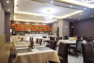 Uma sala de jantar com mesas e cadeiras, cozinha ao fundo, e um design de teto moderno.