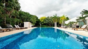 Piscina retangular com água azul cristalina, cercada por espreguiçadeiras e plantas em vasos.