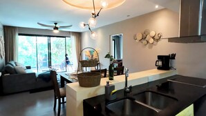 Cozinha moderna com ilha central, pia de aço inoxidável e área de jantar com sofá e mesa.