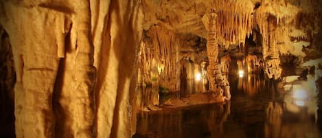 Caverna com estalactites e estalagmites, um corpo d'água e uma fonte de luz.