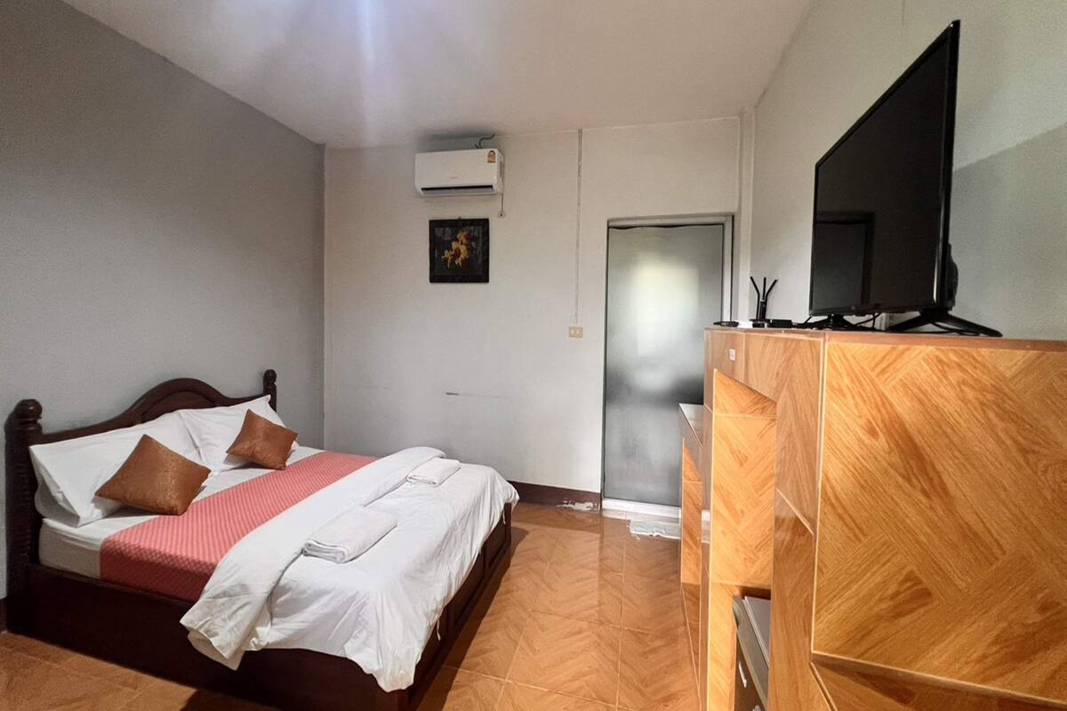 Quarto de hotel com cama, cómoda de madeira, televisão e ar condicionado.