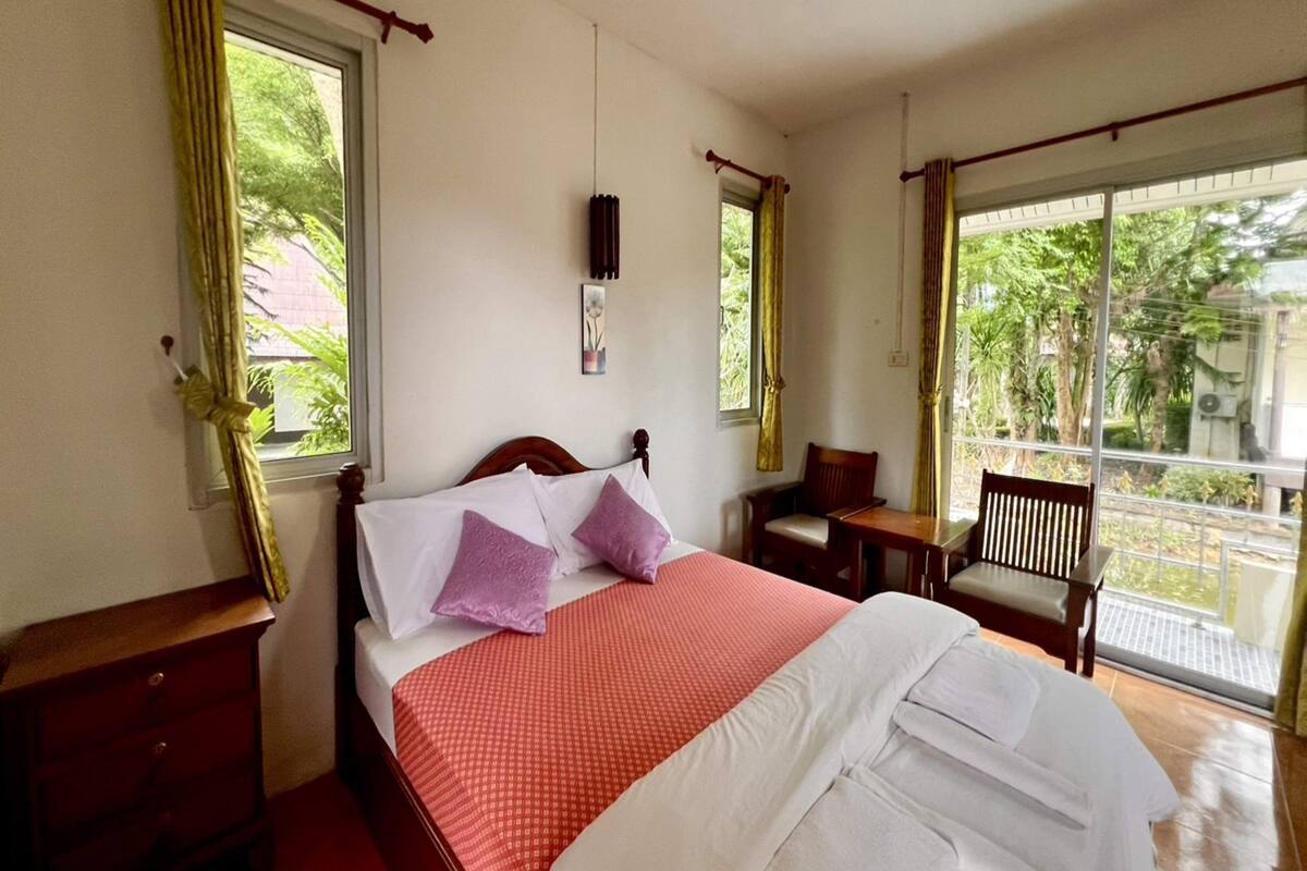 Quarto com cama, duas mesas de cabeceira, um banco de madeira e uma janela com cortinas.