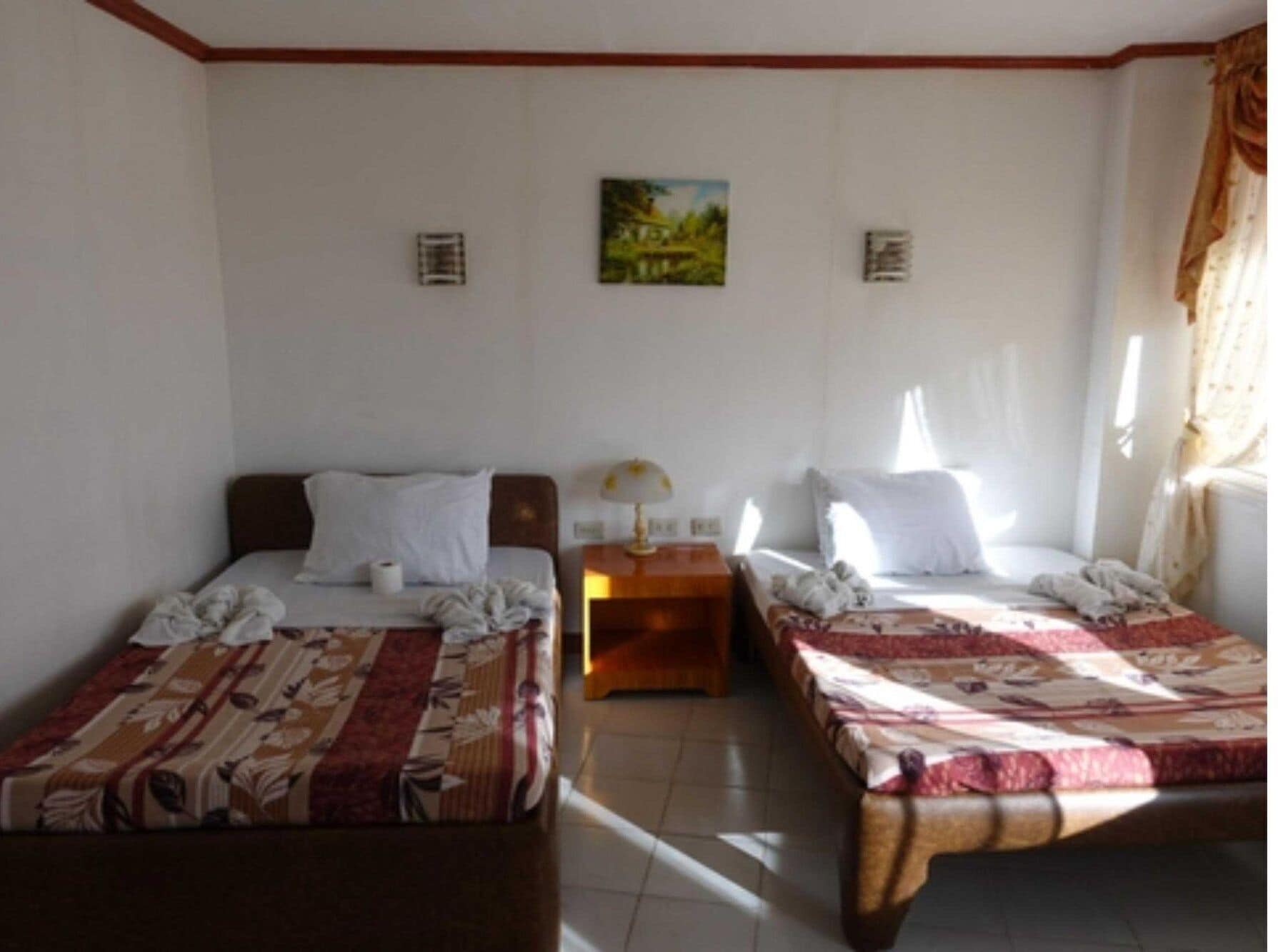 Quarto com duas camas, mesa de cabeceira, luminária e um quadro na parede.