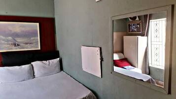 Quarto com uma cama, espelho fixado na parede e um quadro.