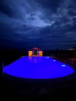 Piscina com área coberta e palco, cercada por uma grade, sob um céu escuro.