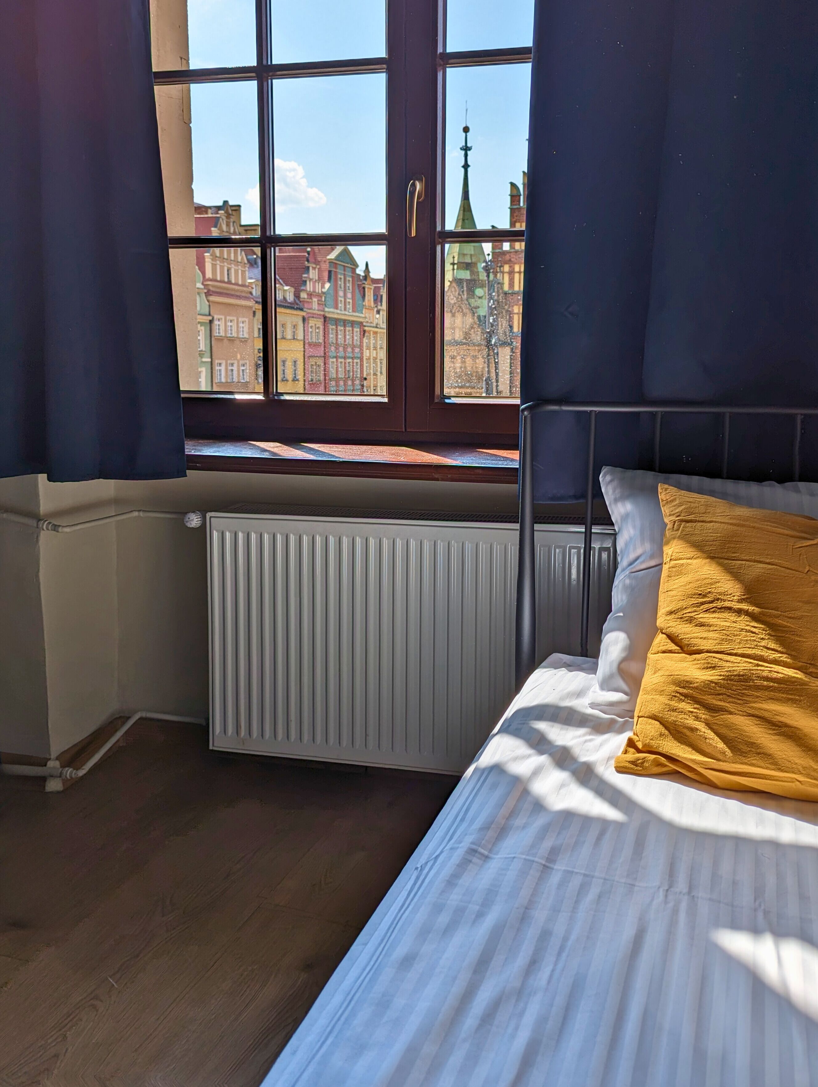 Quarto com cama, radiador e janela com vista para edifícios coloridos.