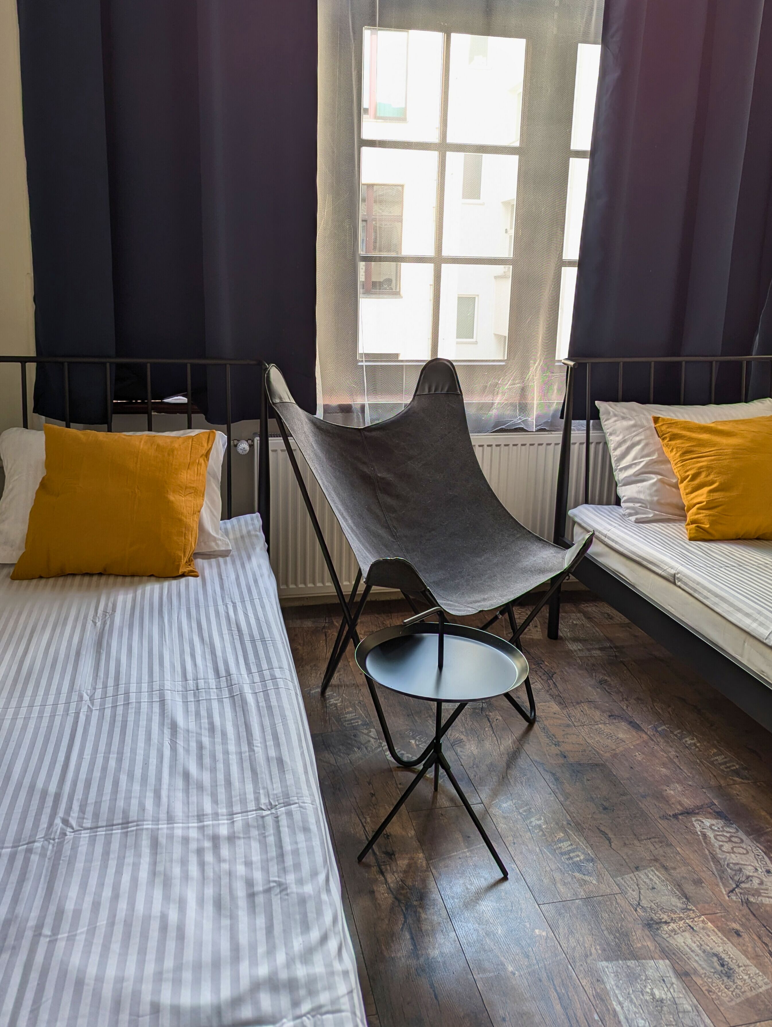 Quarto com duas camas, uma mesa pequena e janela com cortinas.