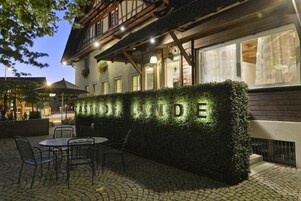 Restaurante com área externa, um conjunto de sebes com texto iluminado e fachada de construção tradicional.