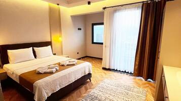 Quarto de hotel com cama, mesa de cabeceira, luminária, janela com cortinas e tapete estampado.