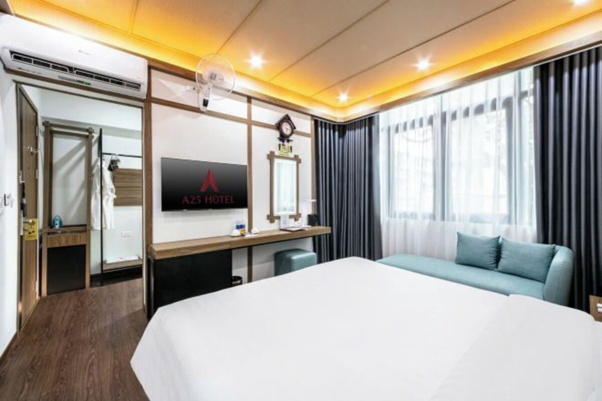Quarto de hotel com cama, escrivaninha, televisão e janela com cortinas.