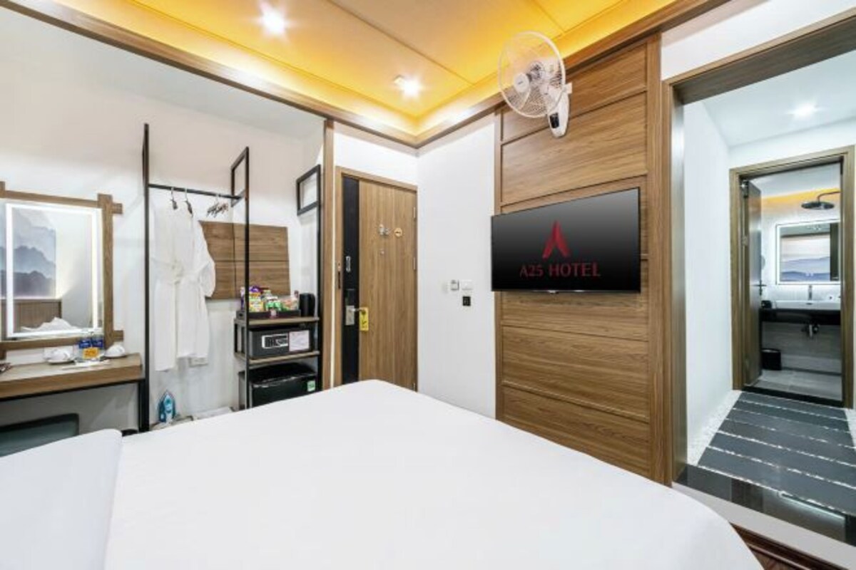 Quarto de hotel com uma cama, guarda-roupa de madeira, televisão e casa de banho visível por uma porta aberta.