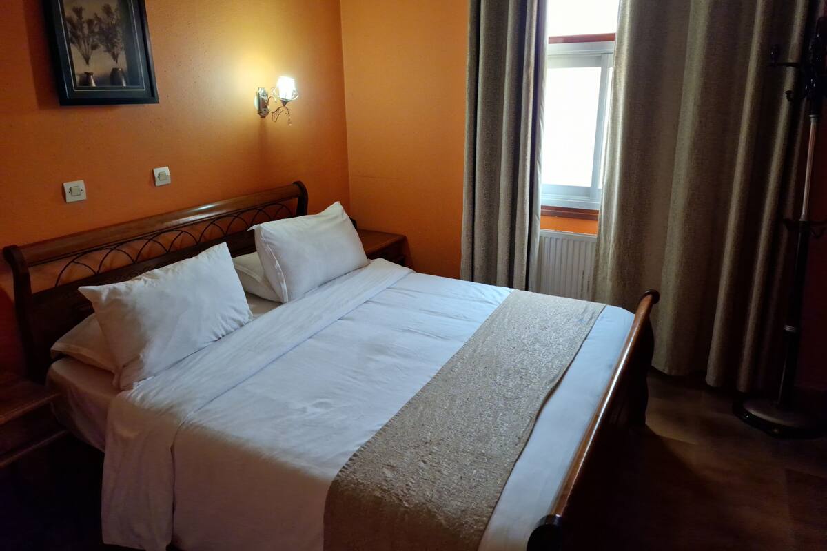 Uma cama bem arrumada com lençóis brancos em um quarto com paredes laranja, um quadro e uma mesa de cabeceira com abajur.