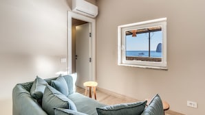 Uma sala de estar moderna com um sofá, uma mesinha redonda e uma janela com vista para o mar.