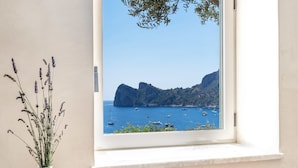 Quarto com grande janela e vista costeira, incluindo barcos e falésias rochosas.