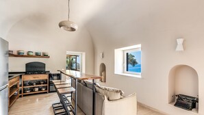 Cozinha espaçosa com mesa de madeira, banquetas de bar e vista para o mar através de uma janela.