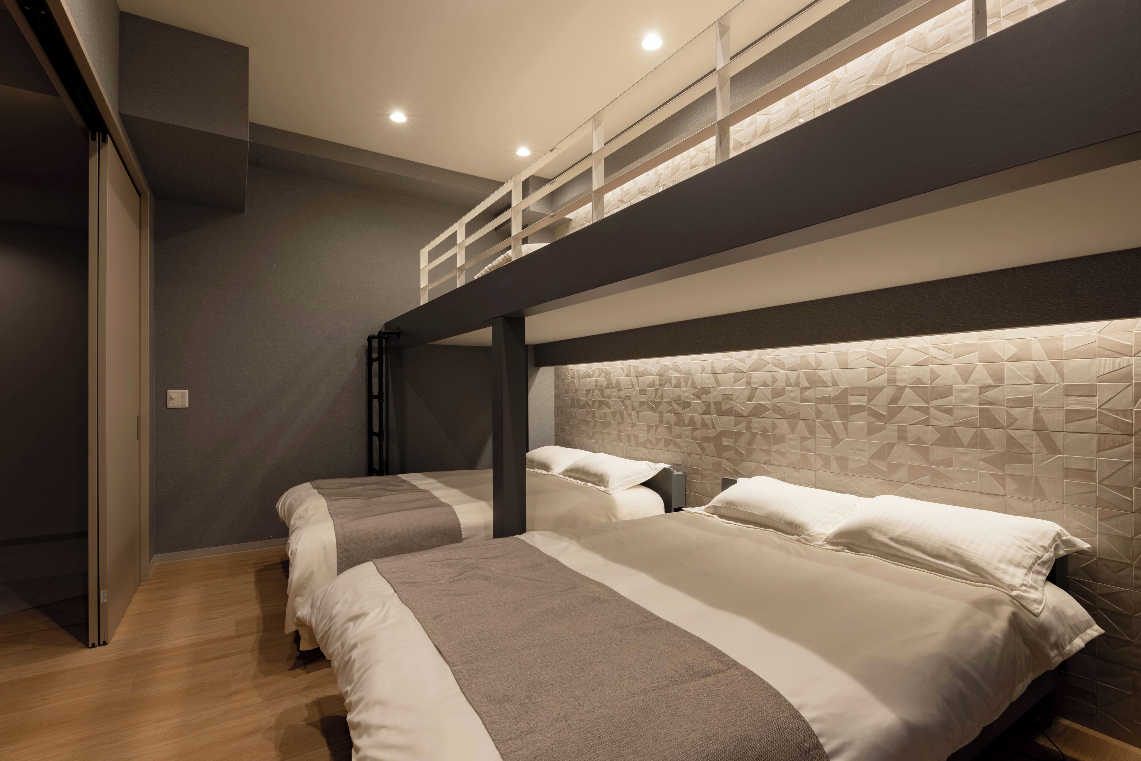 Quarto moderno com duas camas, área de dormir estilo loft e cabeceira com padrão geométrico.