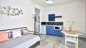 Um apartamento moderno com um sofá cinzento, uma pequena mesa de jantar e uma cozinha com armários azuis e um fogão branco.