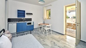 Quarto compacto com cama, pequena cozinha, sala de jantar com mesa e cadeiras, e porta de vidro deslizante para um pátio externo.