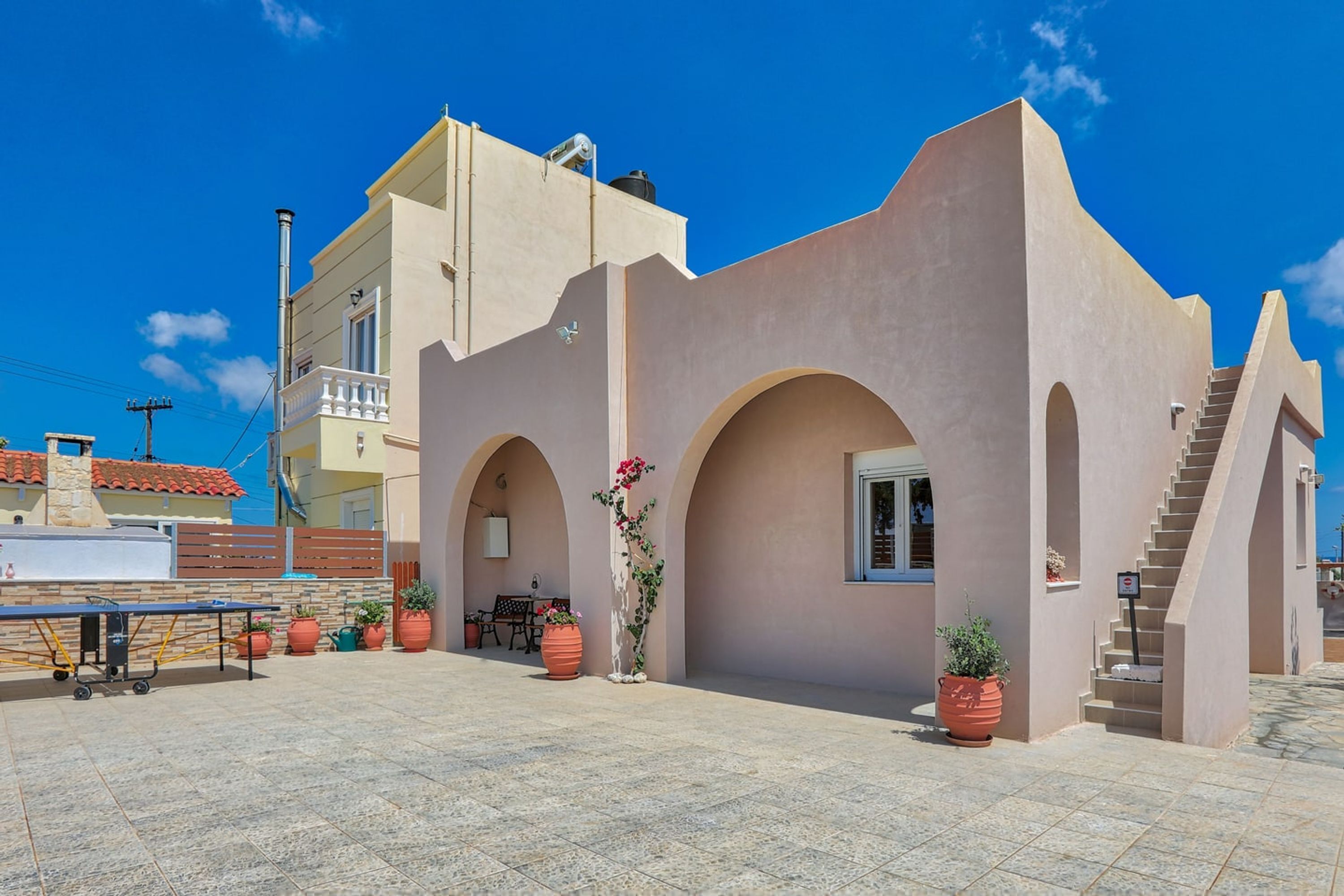 Um edifício com telhado plano, janelas em arco e escadaria que leva à entrada.