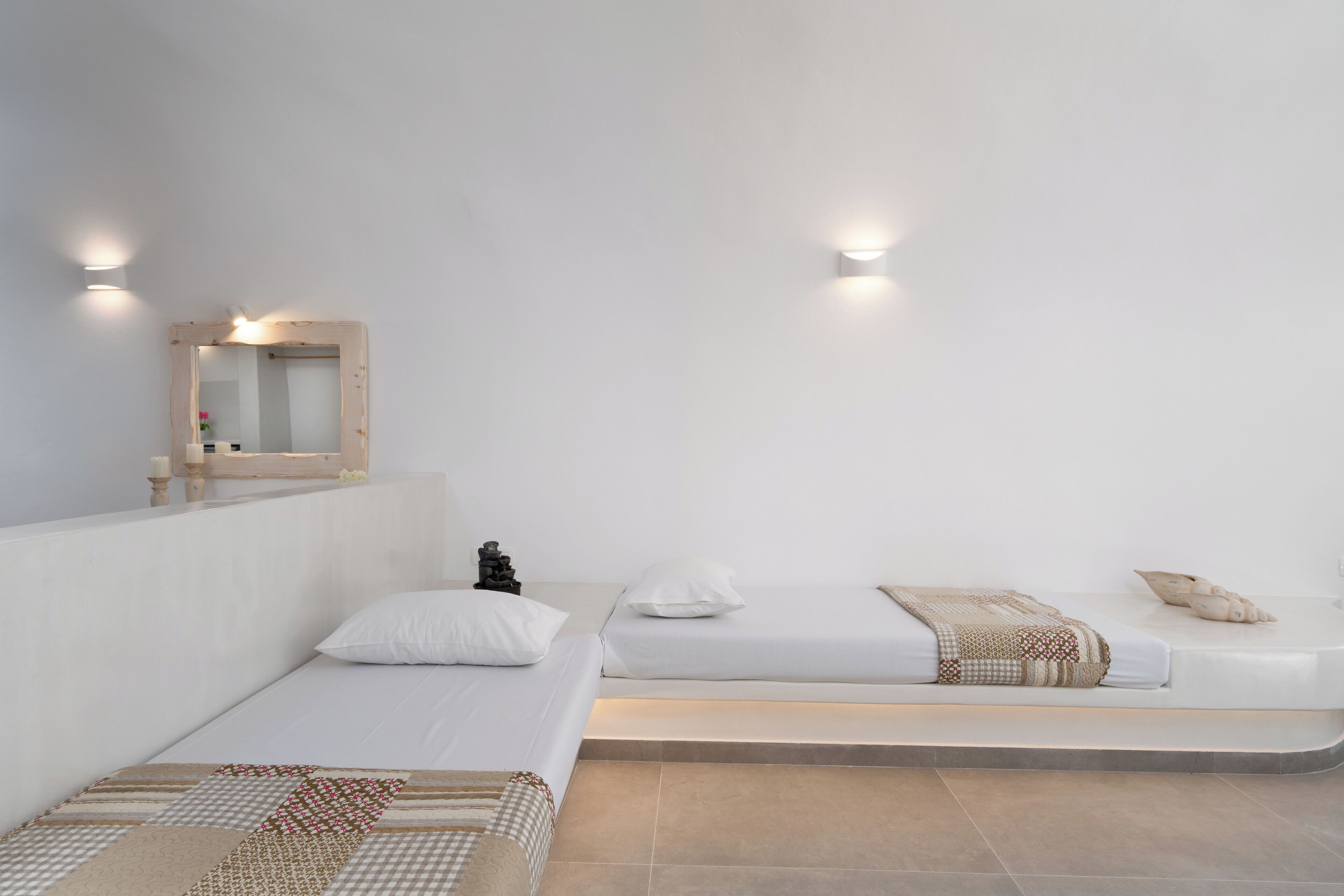 Quarto minimalista com duas camas, um espelho e iluminação embutida na parede.