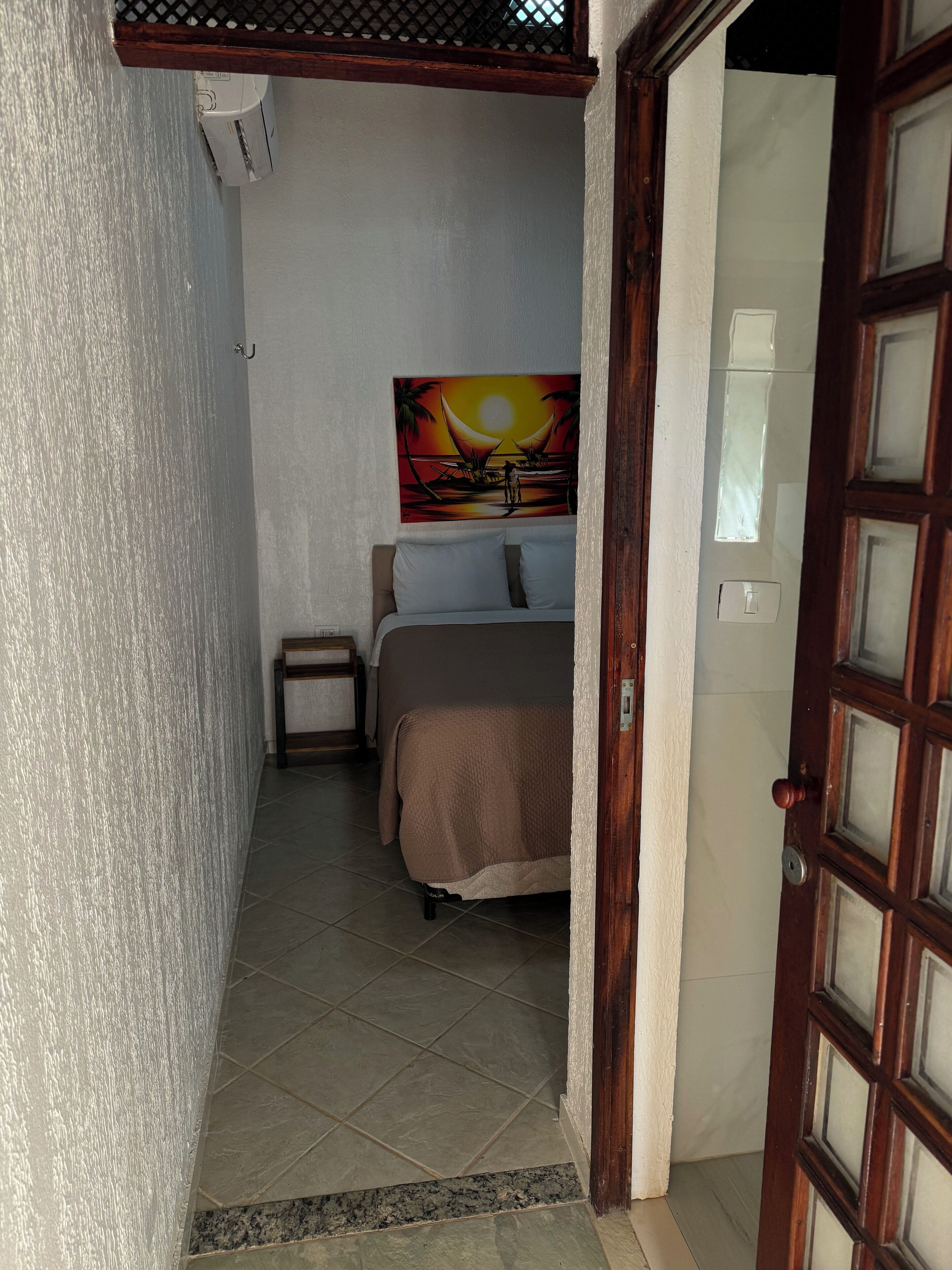 Um corredor estreito com uma cama, uma pequena mesa e um quadro na parede.