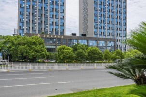 Um edifício moderno com telhado plano e janelas retangulares, rodeado por vegetação e céu claro.