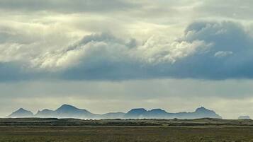 Uma extensa paisagem aberta com colinas ondulantes e montanhas ao longe sob um céu nublado.