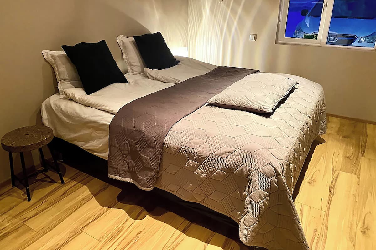 Uma cama com cobertura acolchoada, duas almofadas pretas e um cobertor marrom.